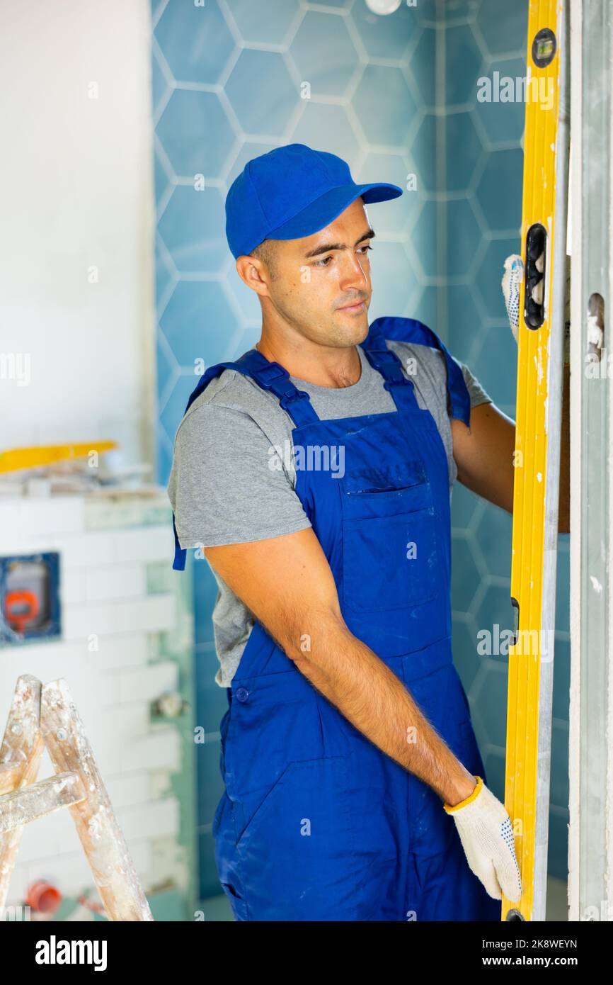 Master wearing work clothes checking vertical of installing tiles using ...