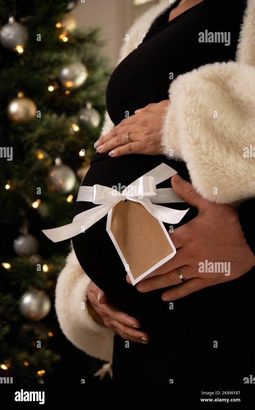 couples hand on pregnant belly, Christmas tree in background Stock ...