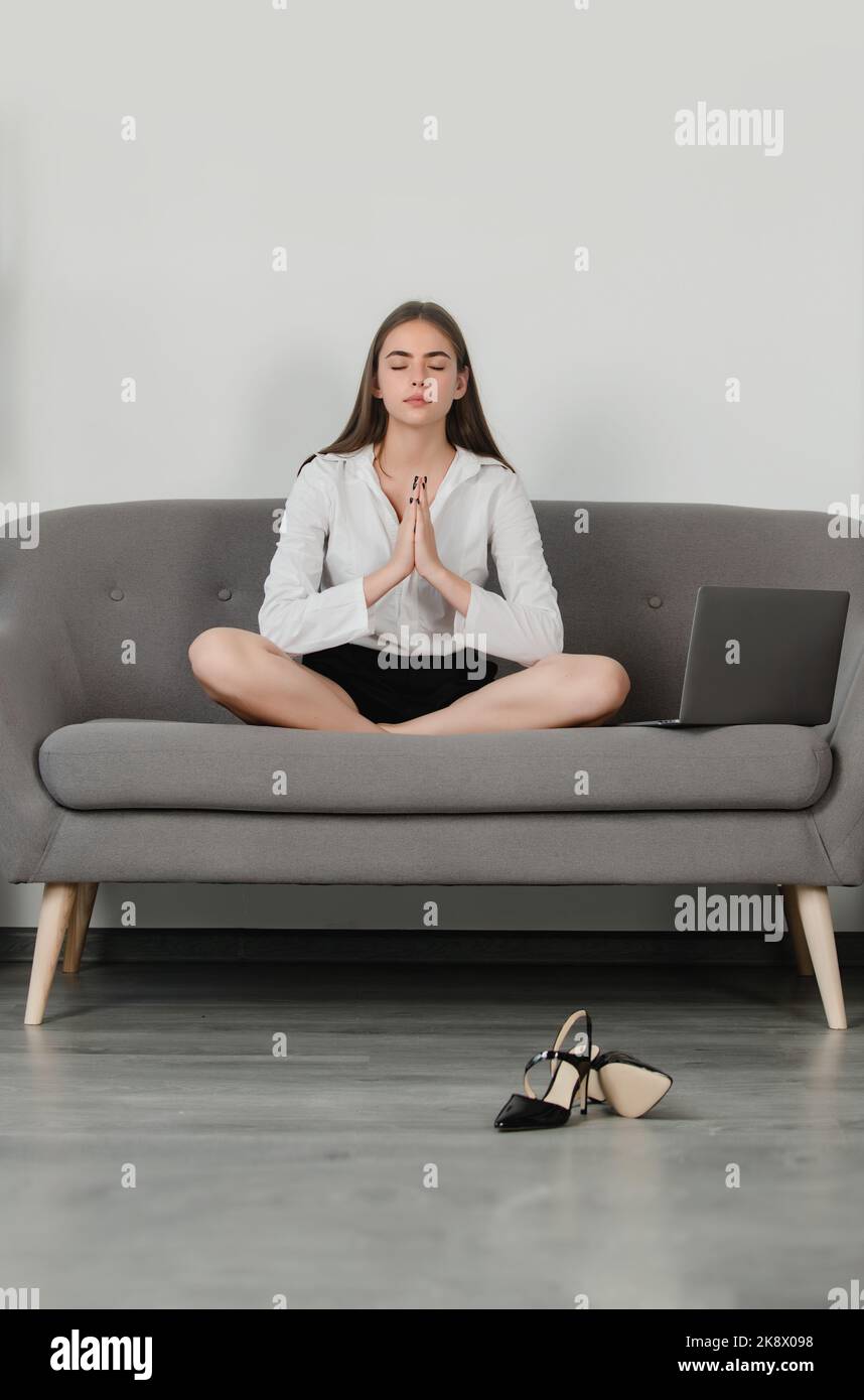 Meditation woman in a modern workplace doing yoga exercise on sofa at ...