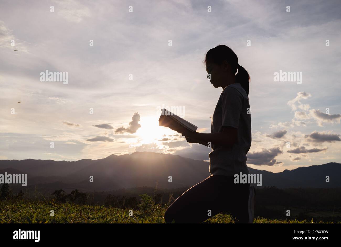 Silhouette of woman praying to god with bible on mountain at sunset ...