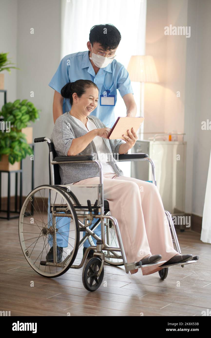 Nursing home worker helping senior woman sitting in wheelchair to video ...