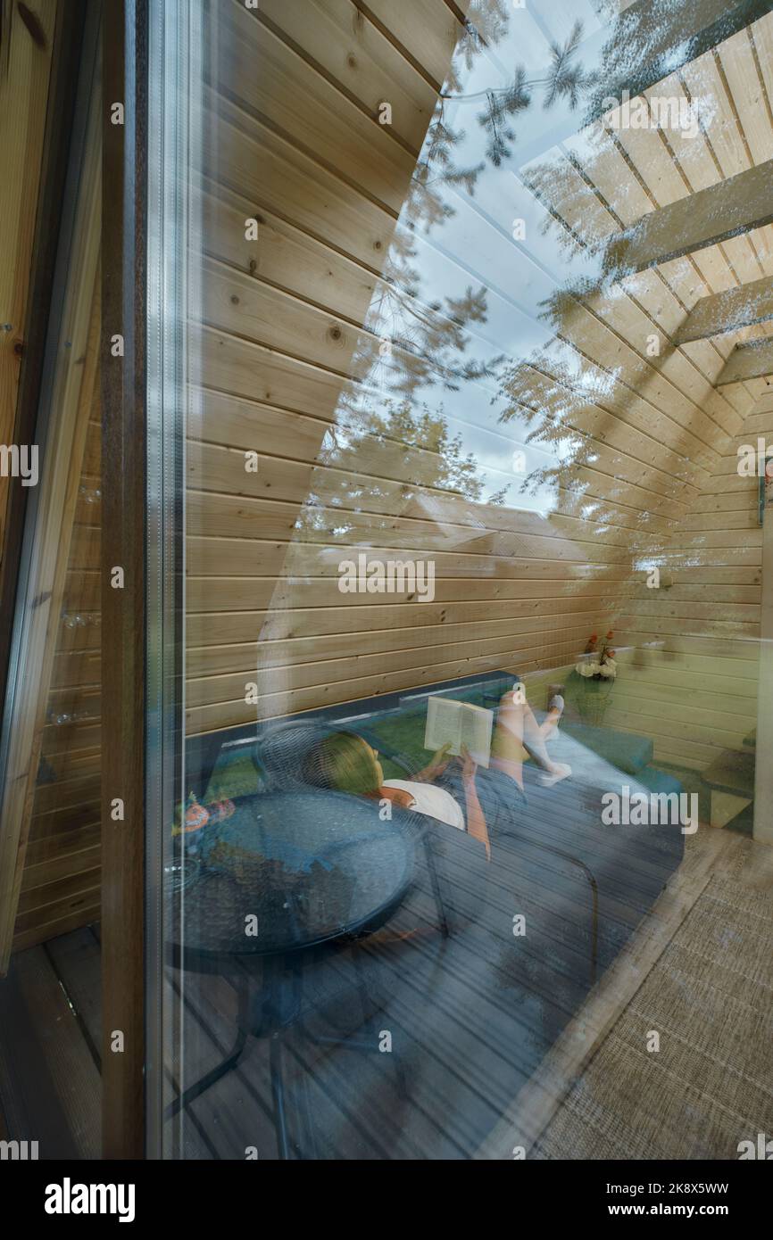 View through the window at young woman on sofa inside summer house ...