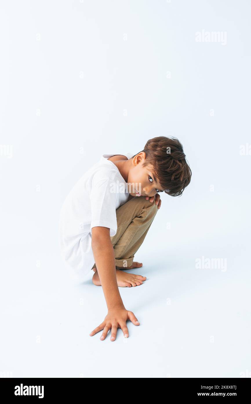 Sulking grim crouching Indian boy looking from under his brow against ...