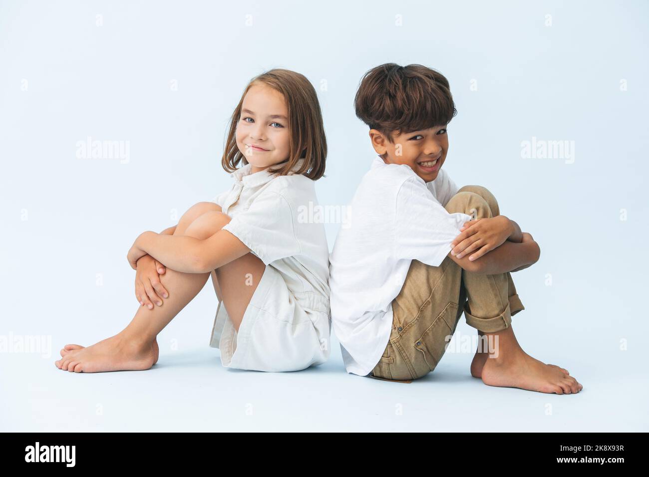 Fun portrait of awkwardly smiling boy and girl sitting back to back on ...