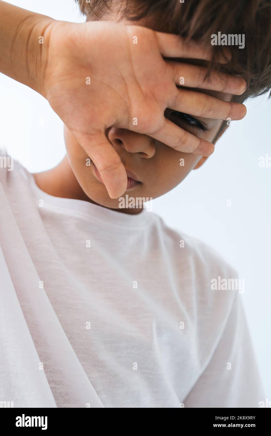 Sad Indian boy covering his face with a hand against bluish white background Stock Photo - Alamy