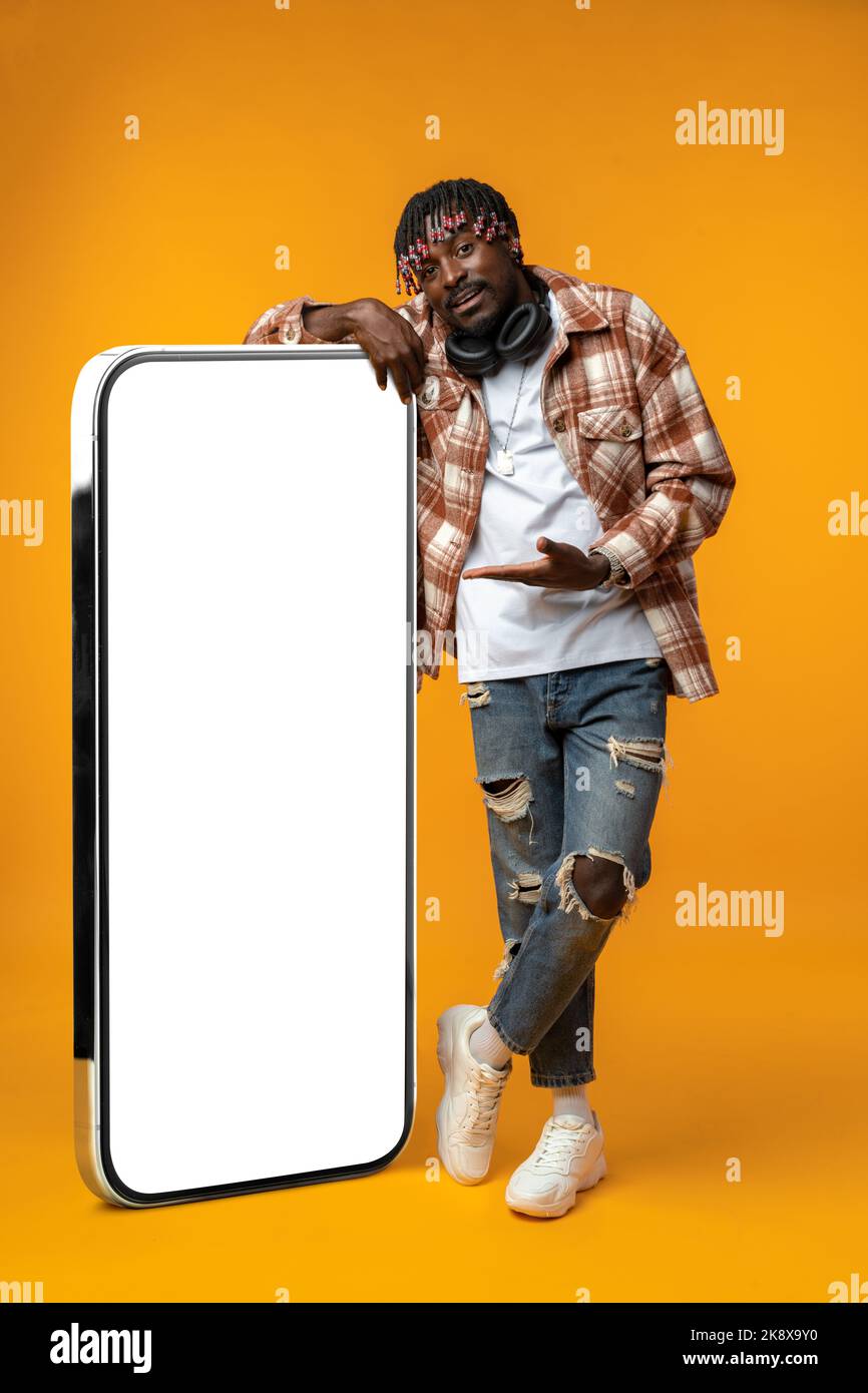 Smiling african man standing near huge smartphone with blank screen on ...