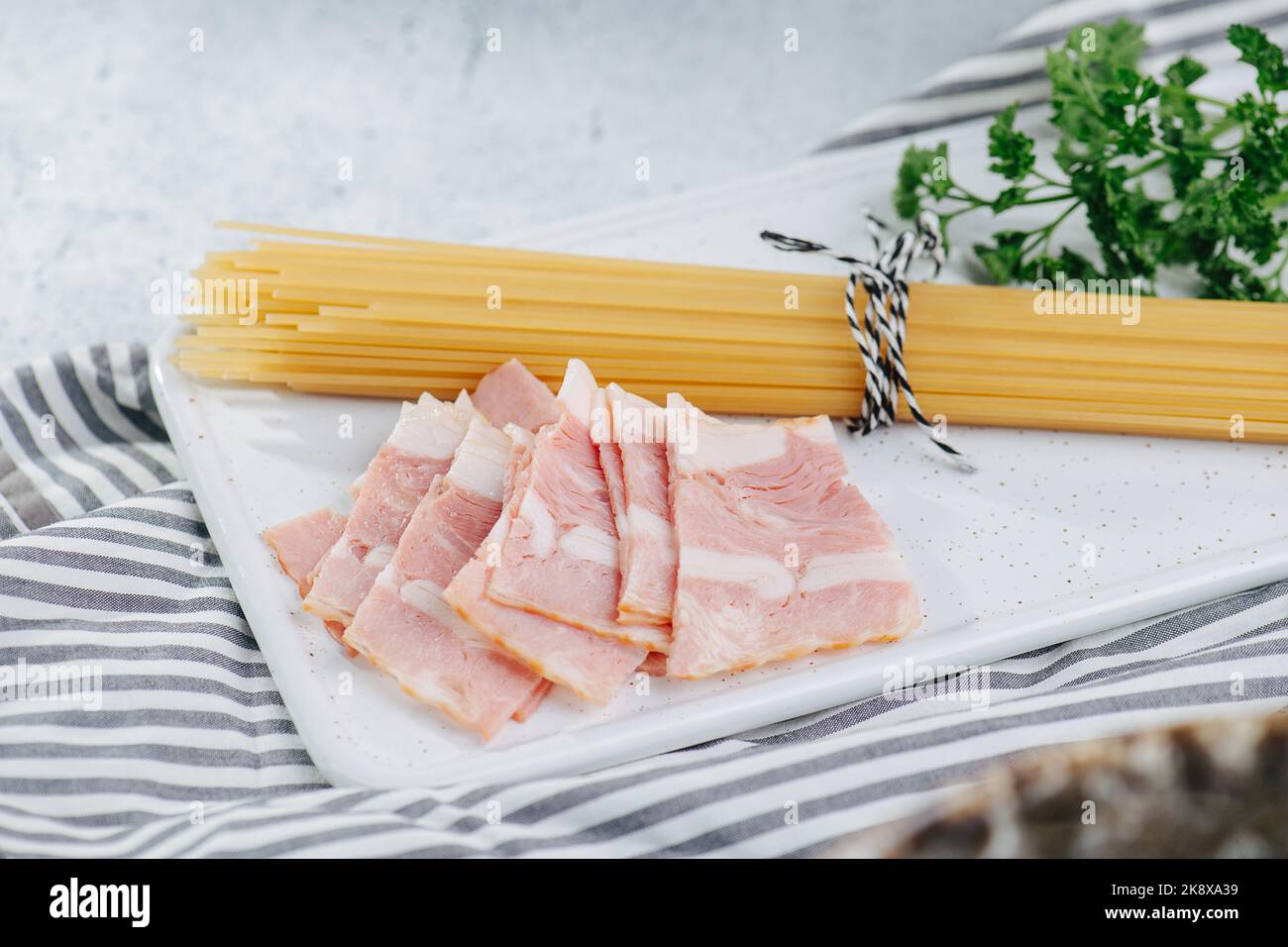 Raw ham, dry spaghetti and some greens on a cloth on a table Stock ...