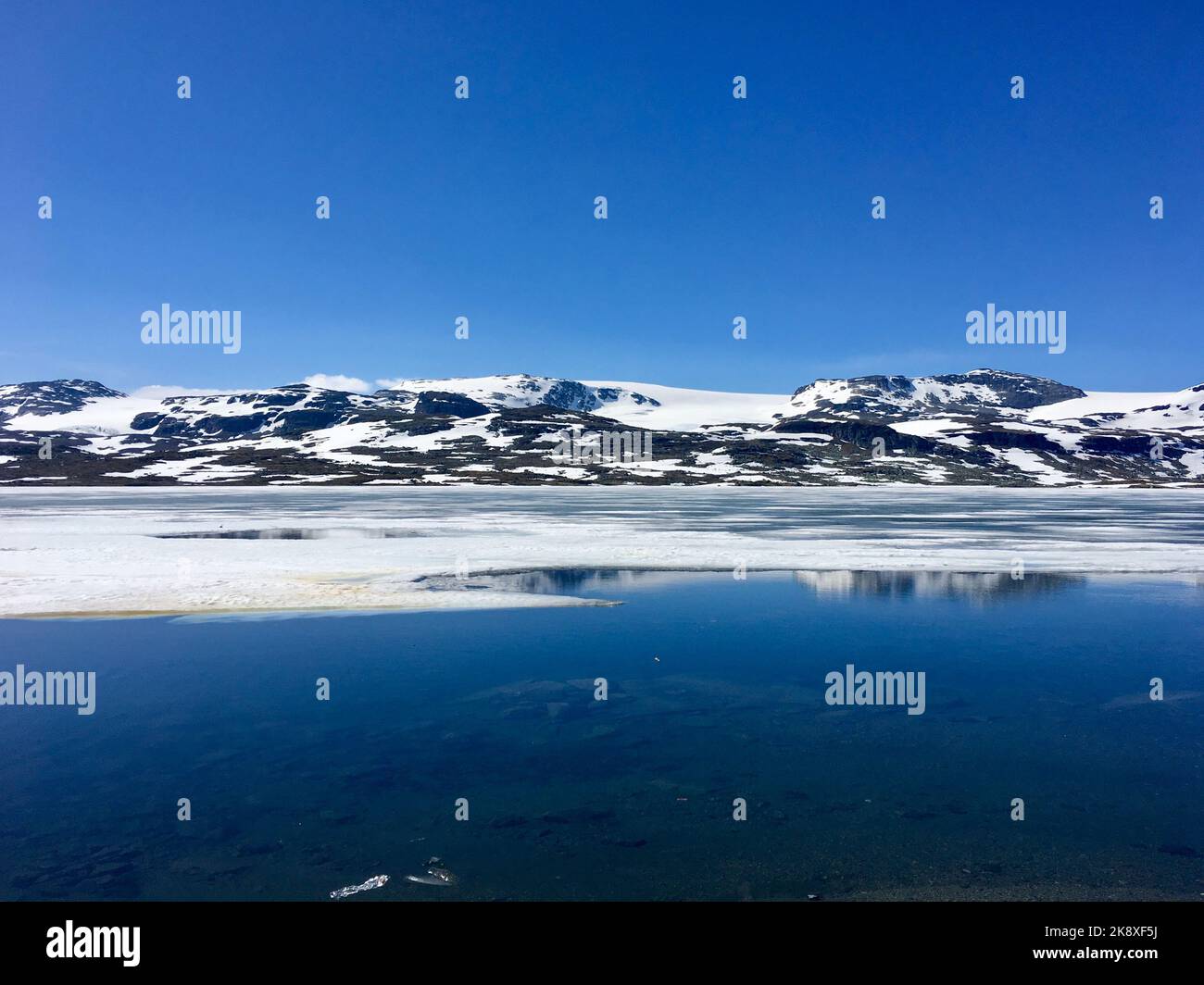 A beautiful frozen lake with wide rocky mountains in the background ...
