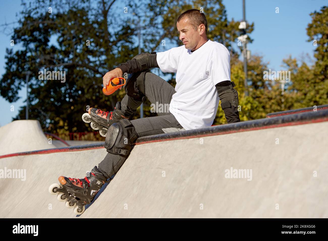 Young man in white t-shirt and jeans wearing rollerblades sitting on ...