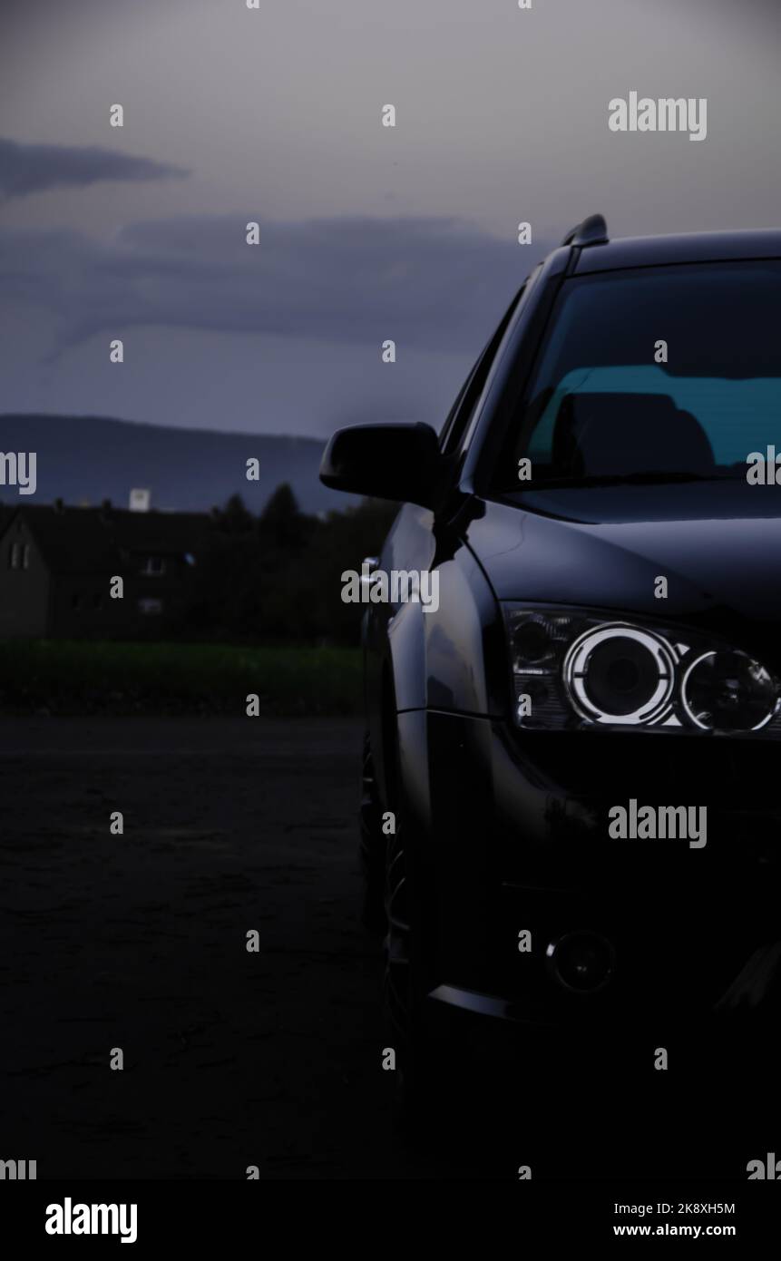 A front view shot of a shiny luxury car outdoors under dark sunset sky ...