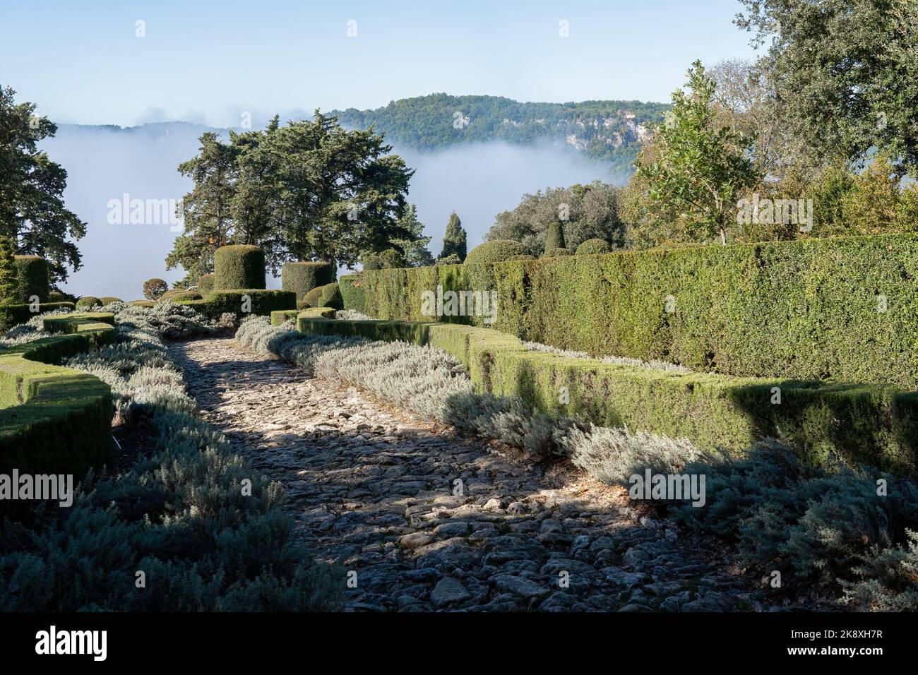 a stone pathway leads down between autumn flower borders and topiary ...