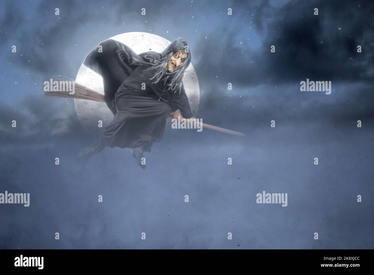 Old witch in a cloak flying on a broomstick in the night with full moon ...