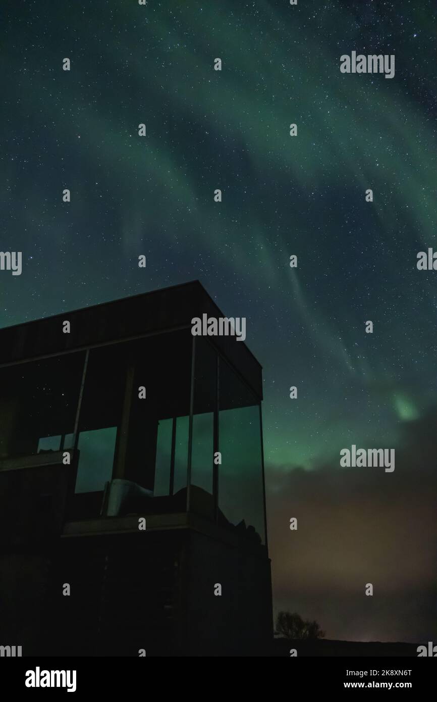 A vertical low angle shot of the green Northern lights over a modern ...