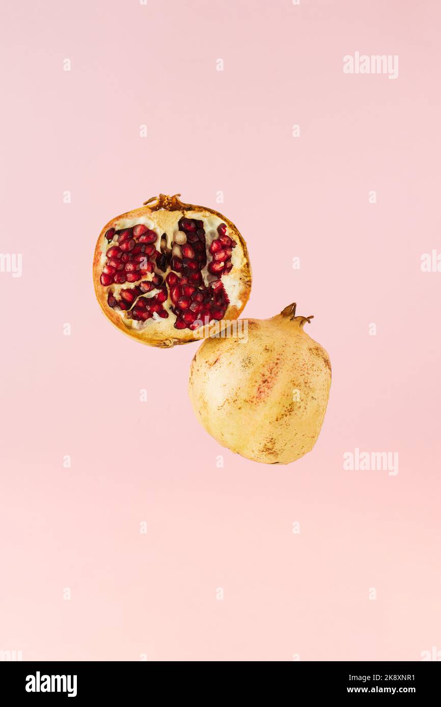 Fresh pomegranate cut in half levitating against pink background. Copy ...