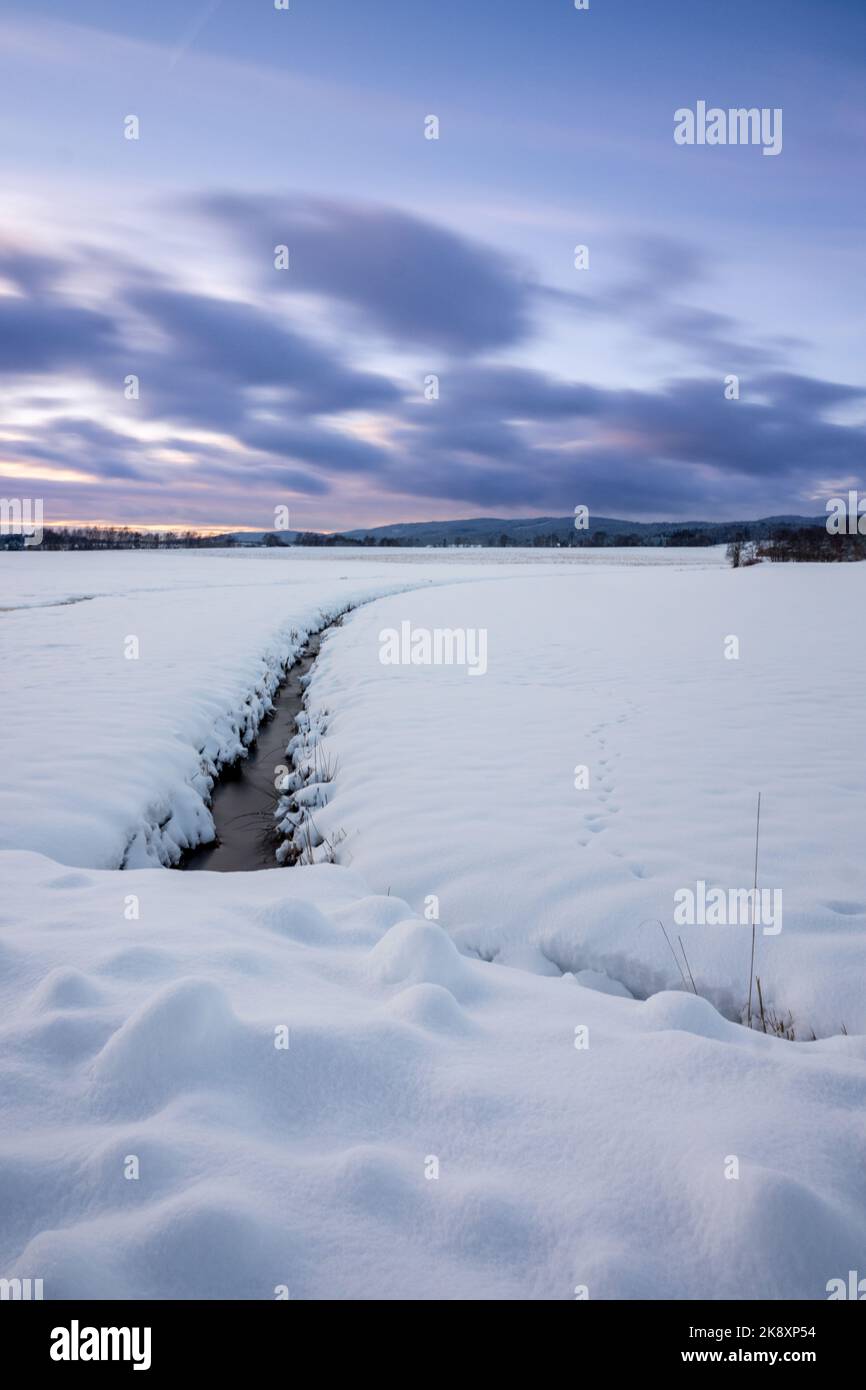 A vertical shot of a narrow river stream passing through an open field ...