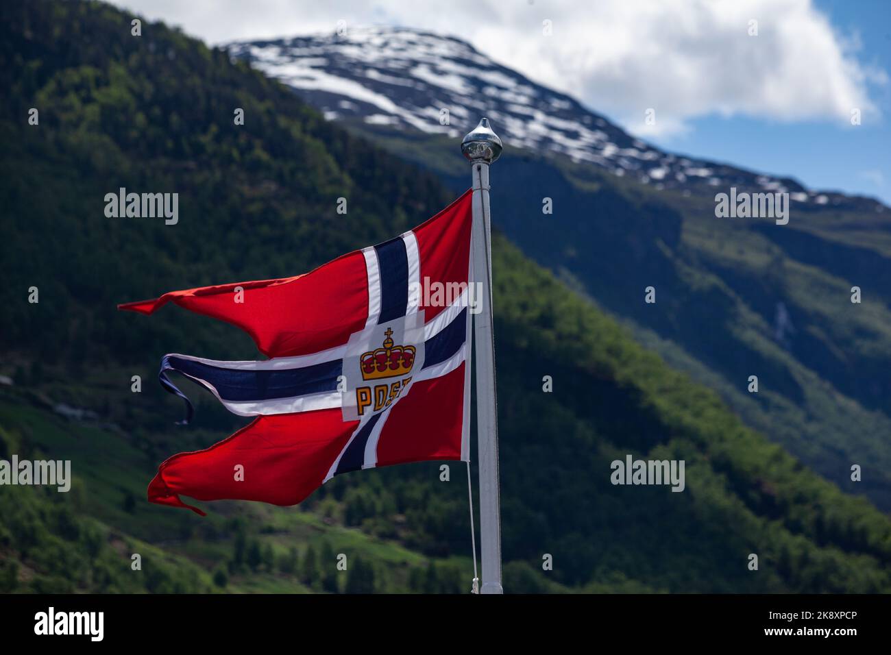 A red Norway flag waving in the wind surrunded by mountains in Narrow ...