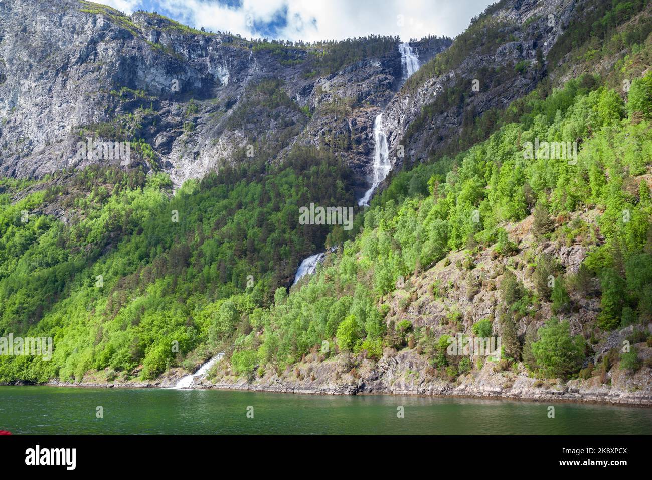 A Narrow Fjord surrounded by mountains with a waterfall in Vestland ...