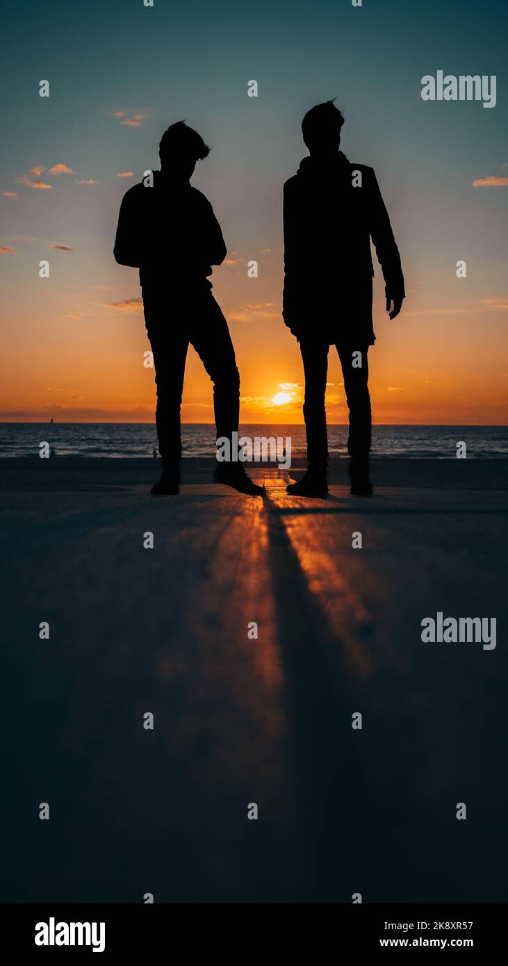 A silhouette of two men in the background of orange sunset scene over ...