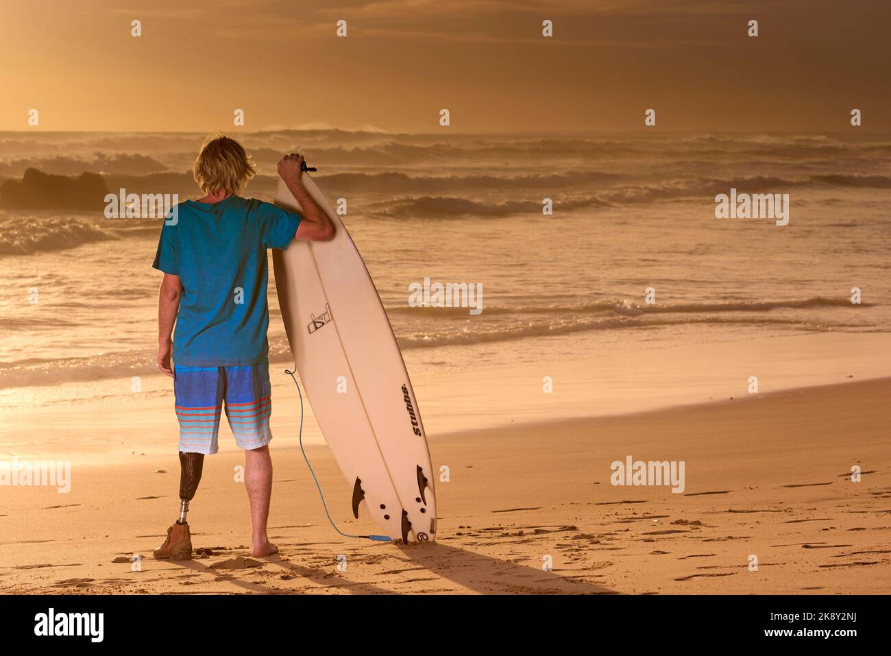 One legged disabled surfer wearing prosthetic leg on beach looking at ...