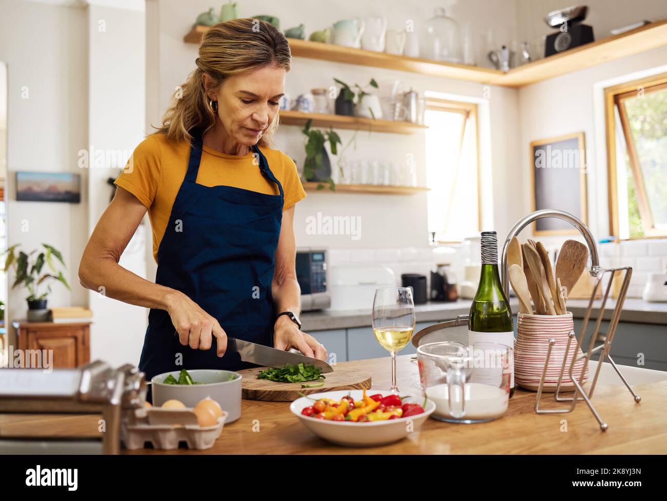 Mature woman, cooking and cutting salad leaf in house and home kitchen ...
