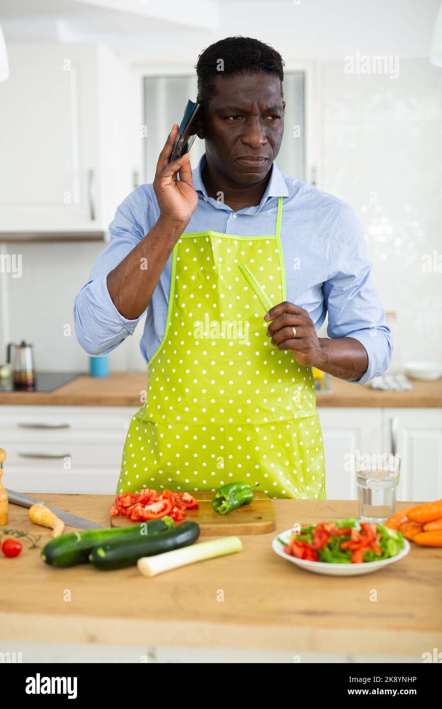 Man in apron talking on phone making dinner at kitchen table Stock ...