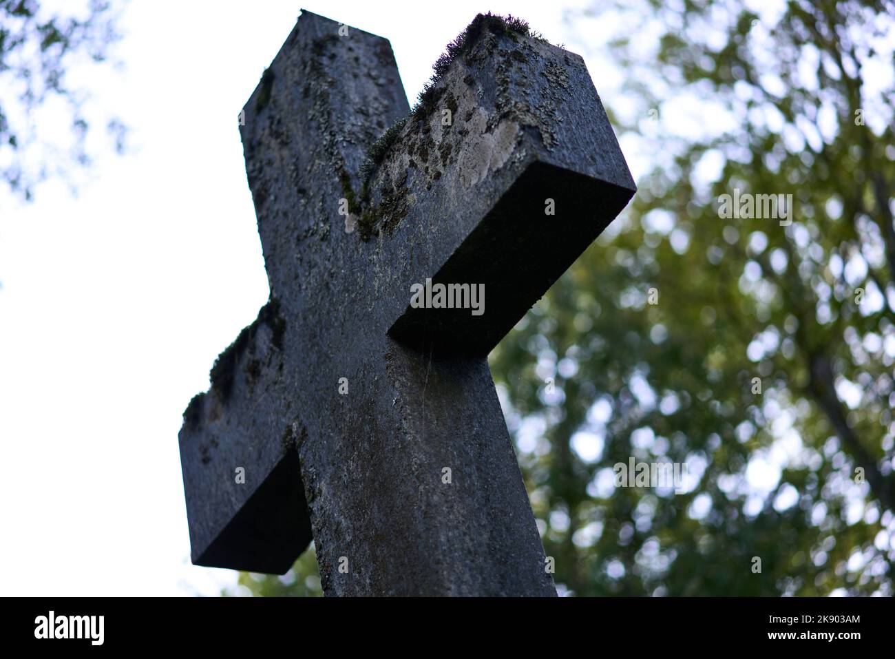 A low-angle shot of a concrete cross covered in moss in an old cemetery ...