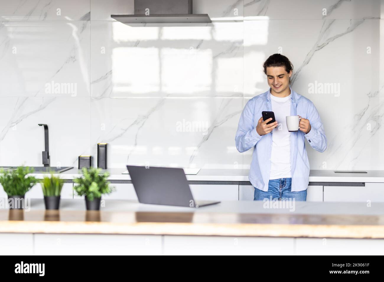 Young man using smartphone, cooking salad in modern kitchen, searching ...