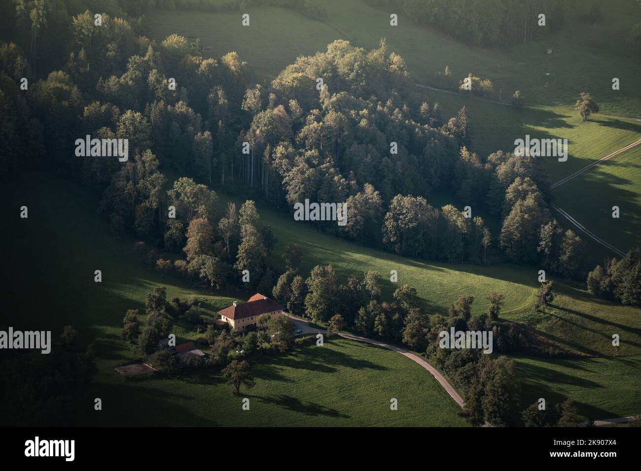 A single, countryside house surrounded by pasture and dense forest ...