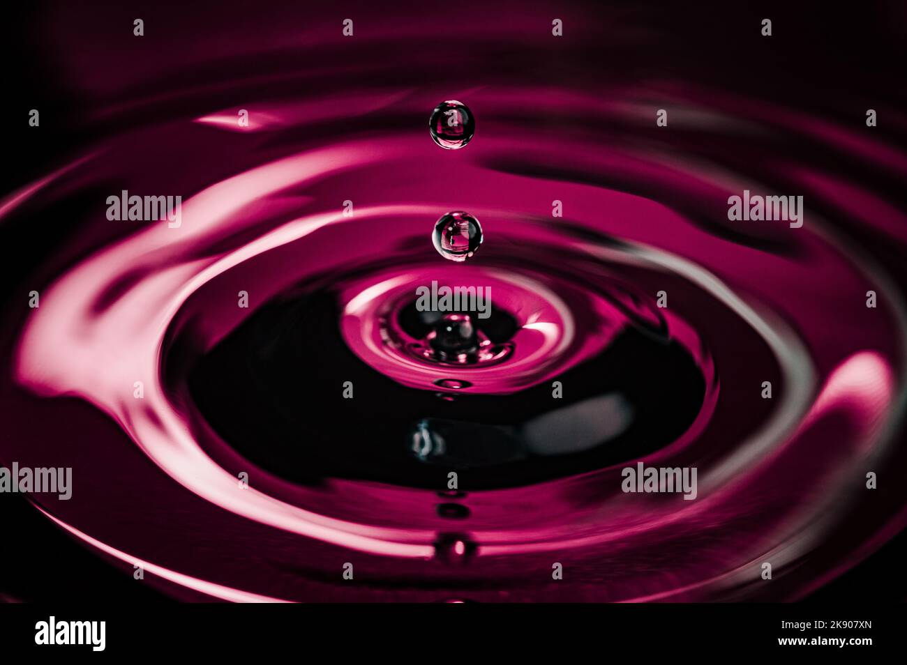 The close-up view of water drops dripping into a dark pink liquid Stock ...