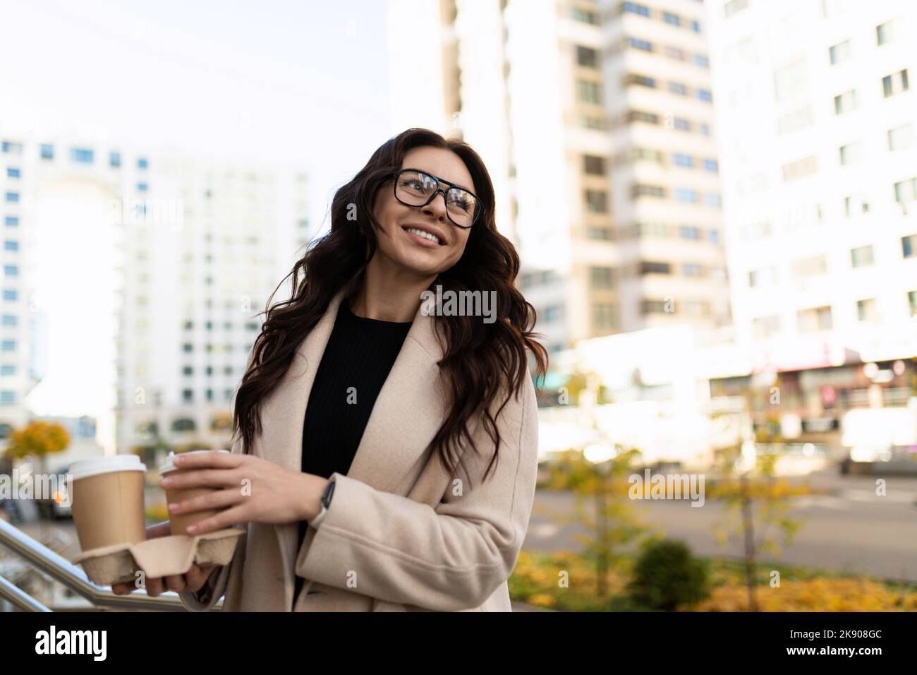 stylish and satisfied businesswoman with cups of coffee in her hands on ...