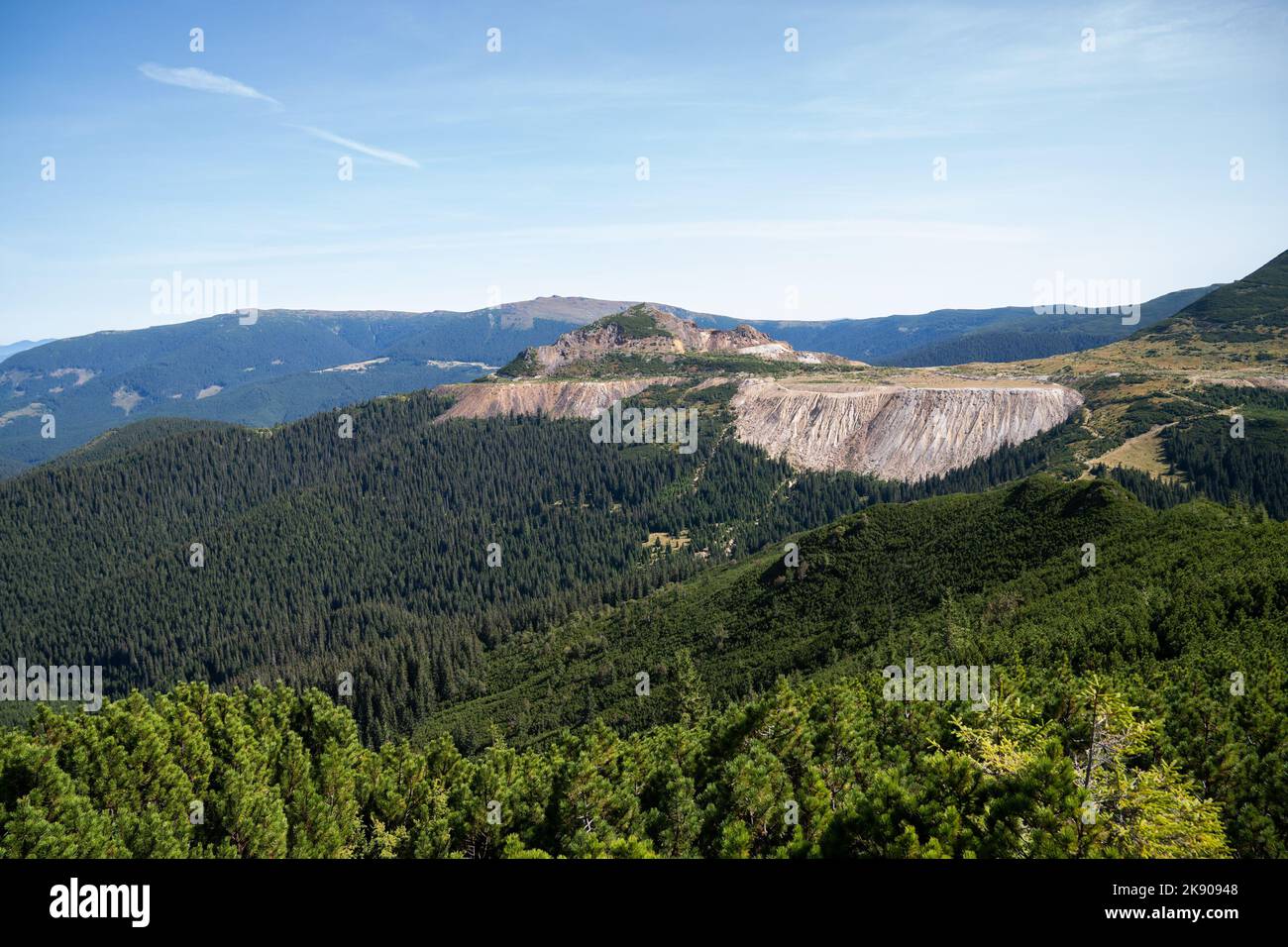 A stunning view of layered mountain ranges covered with dense pine forests under blue sky on ...