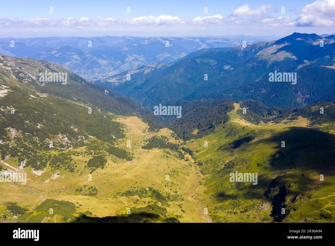 Stunning view of blue cloudy sky over layered mountain ranges and valley covered with vegetation ...