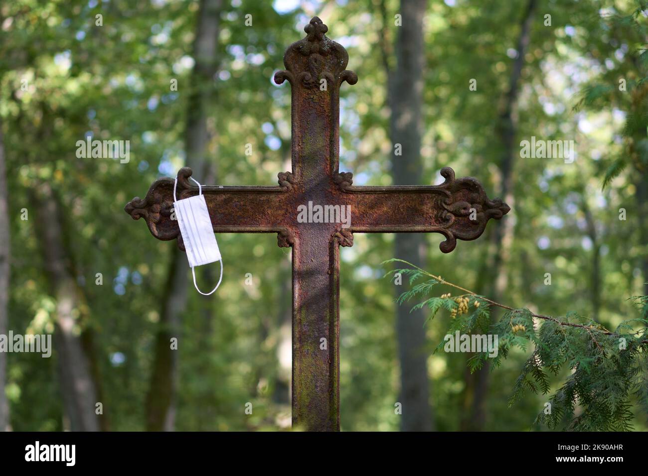 A selective focus shot of a rusty metal cross with a facemask hanging ...