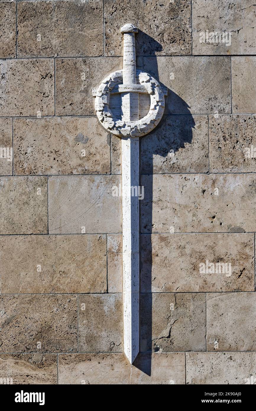A vertical shot of a white sword with a wreath on a stone wall at the ...