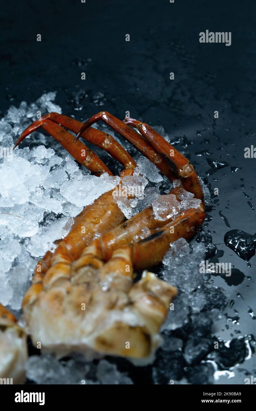 A vertical shot of sliced pieces of a crab on ice isolated on a dark ...