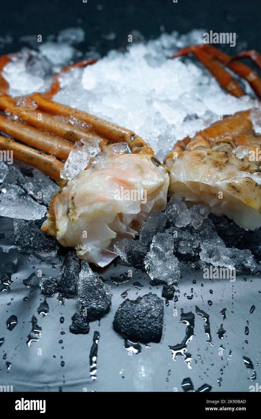 A vertical shot of sliced pieces of a crab on ice isolated on a dark ...