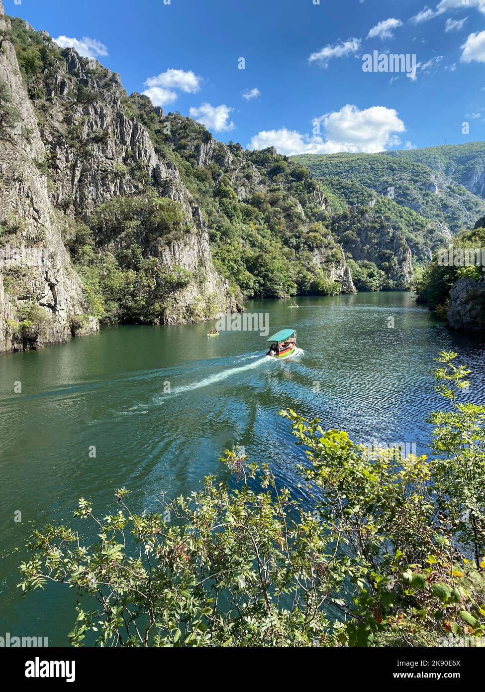 A vertical shot of the river with a boat surrounded by green cliffs ...