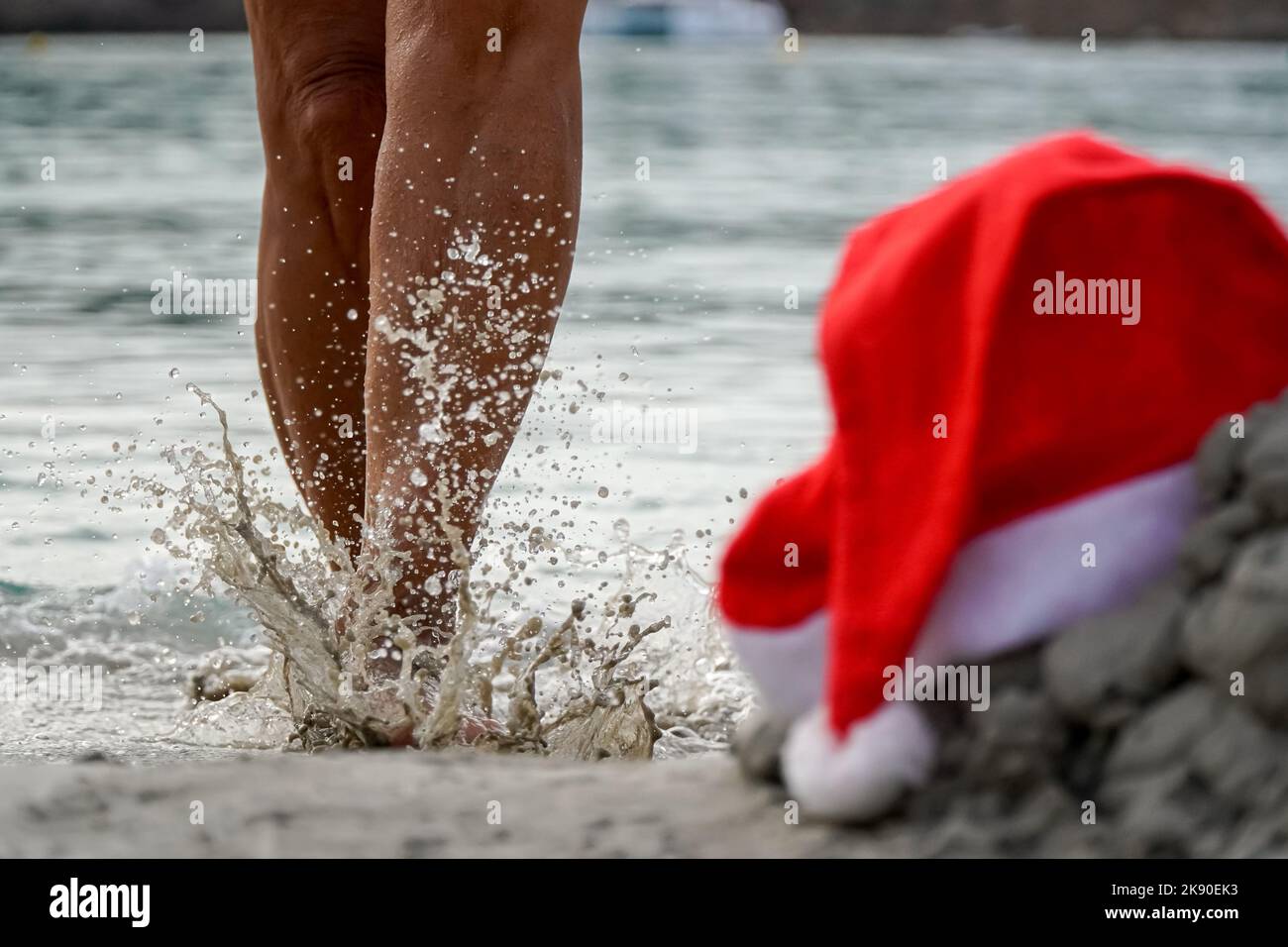 Legs splashing in the water with a Santa hat on the sand. christmas ...