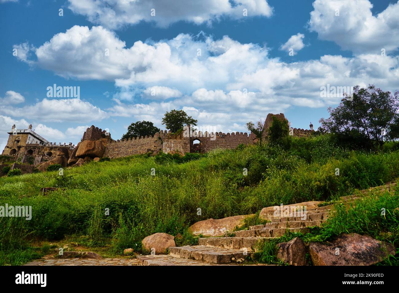 A low-angle of Golconda Fort ruins with grass around and cloudy sky ...