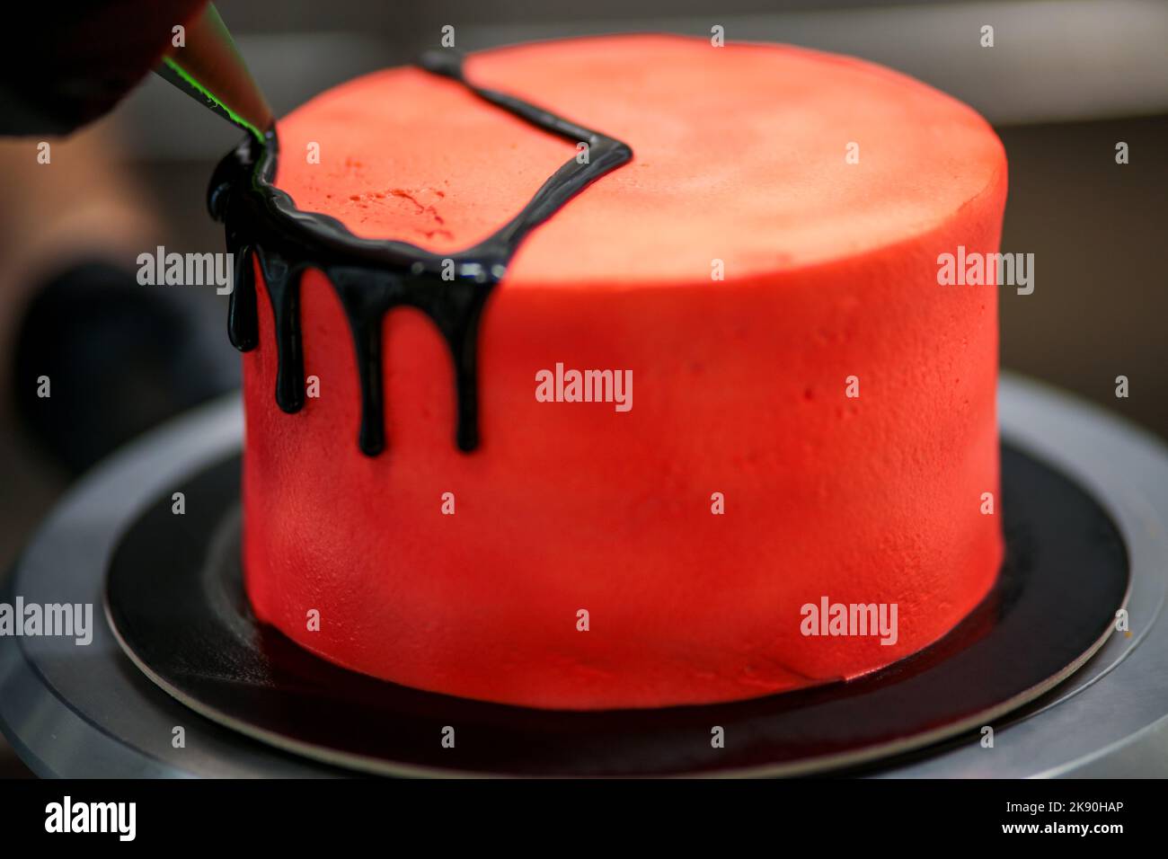 topping a red cake with black dark chocolate icing Stock Photo - Alamy