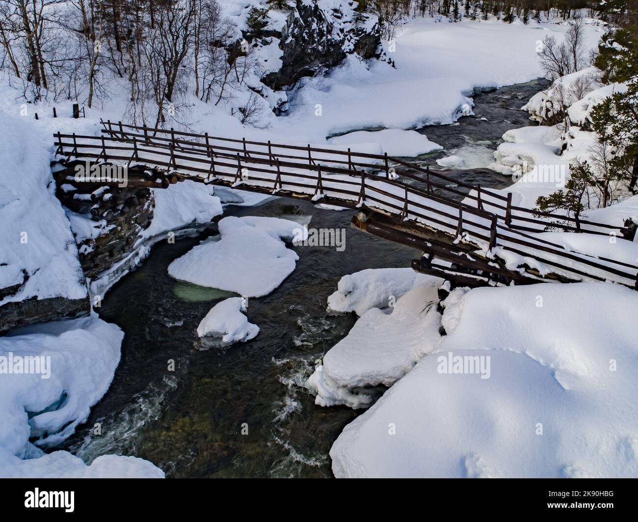 An aerial view of a frozen bridge over a flowing stream in a snowy ...