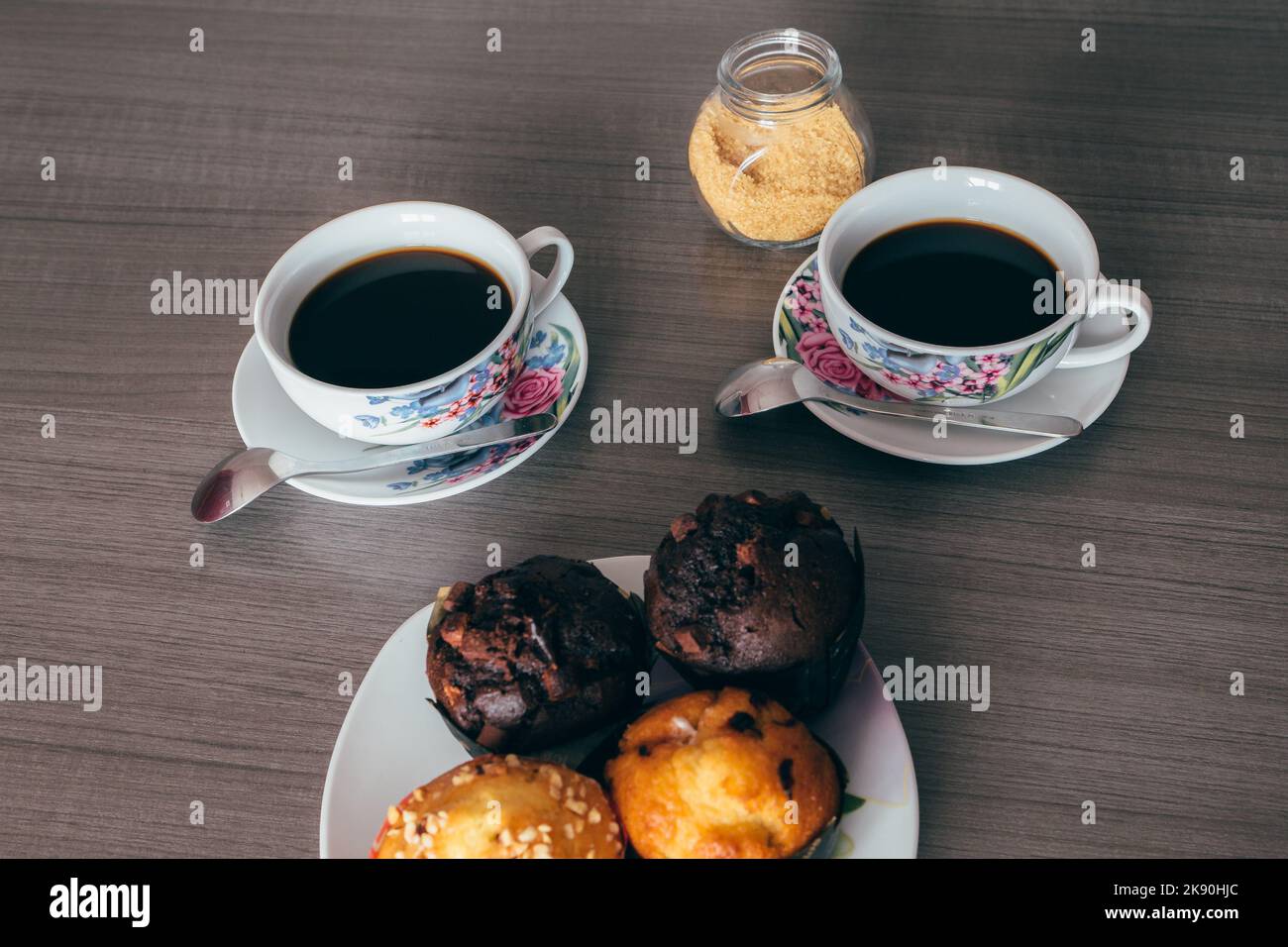 A top view shot of two black teacups with muffins on a plate on a brown ...