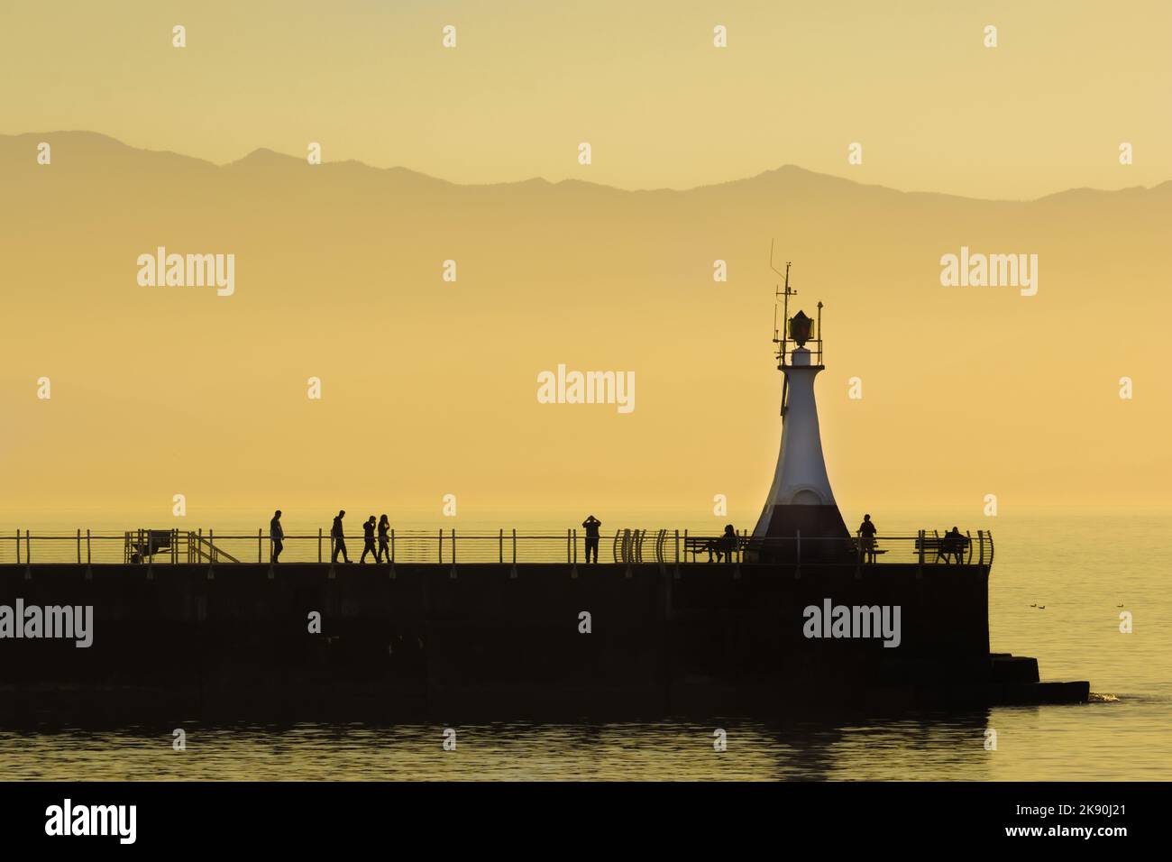 A silhouette of people on Ogden Point breakwater lighthouse in Victoria ...
