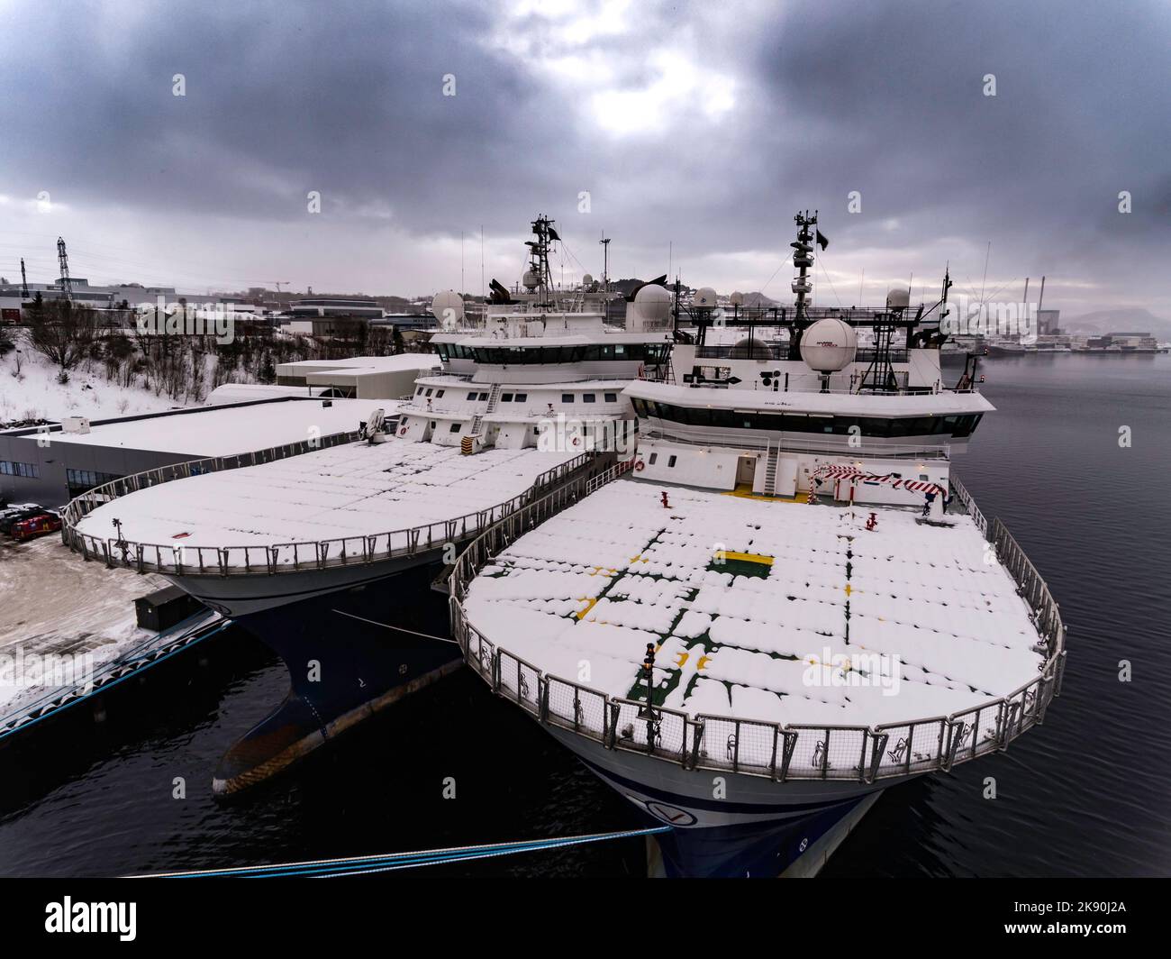 An aerial view of white offshore vessels alongside the shore covered in ...