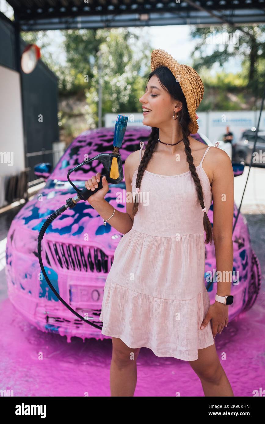Young woman hose stands in front of a car covered in pink foam Stock ...