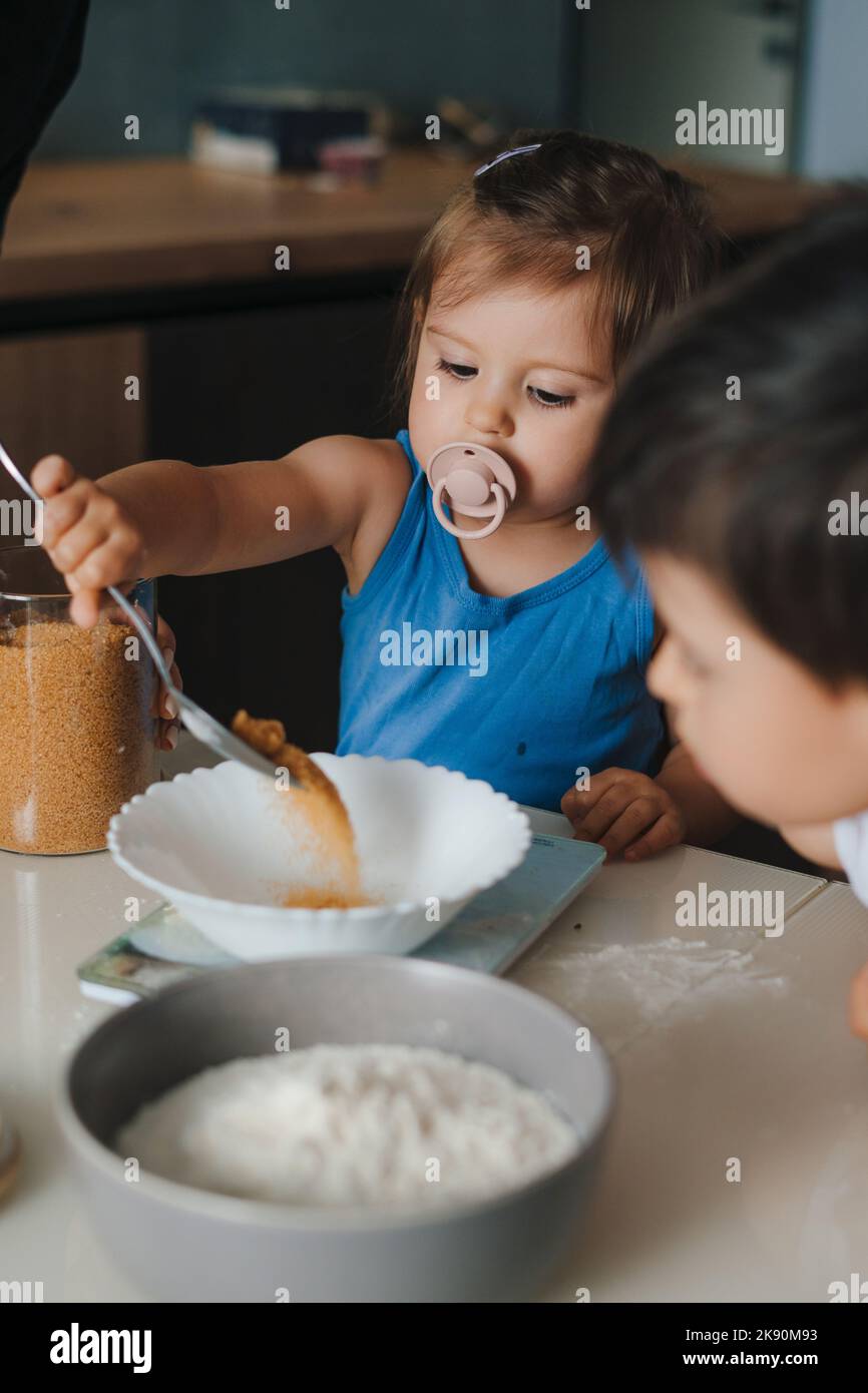 Little girl with her brother spending quality time weighing ingredients ...