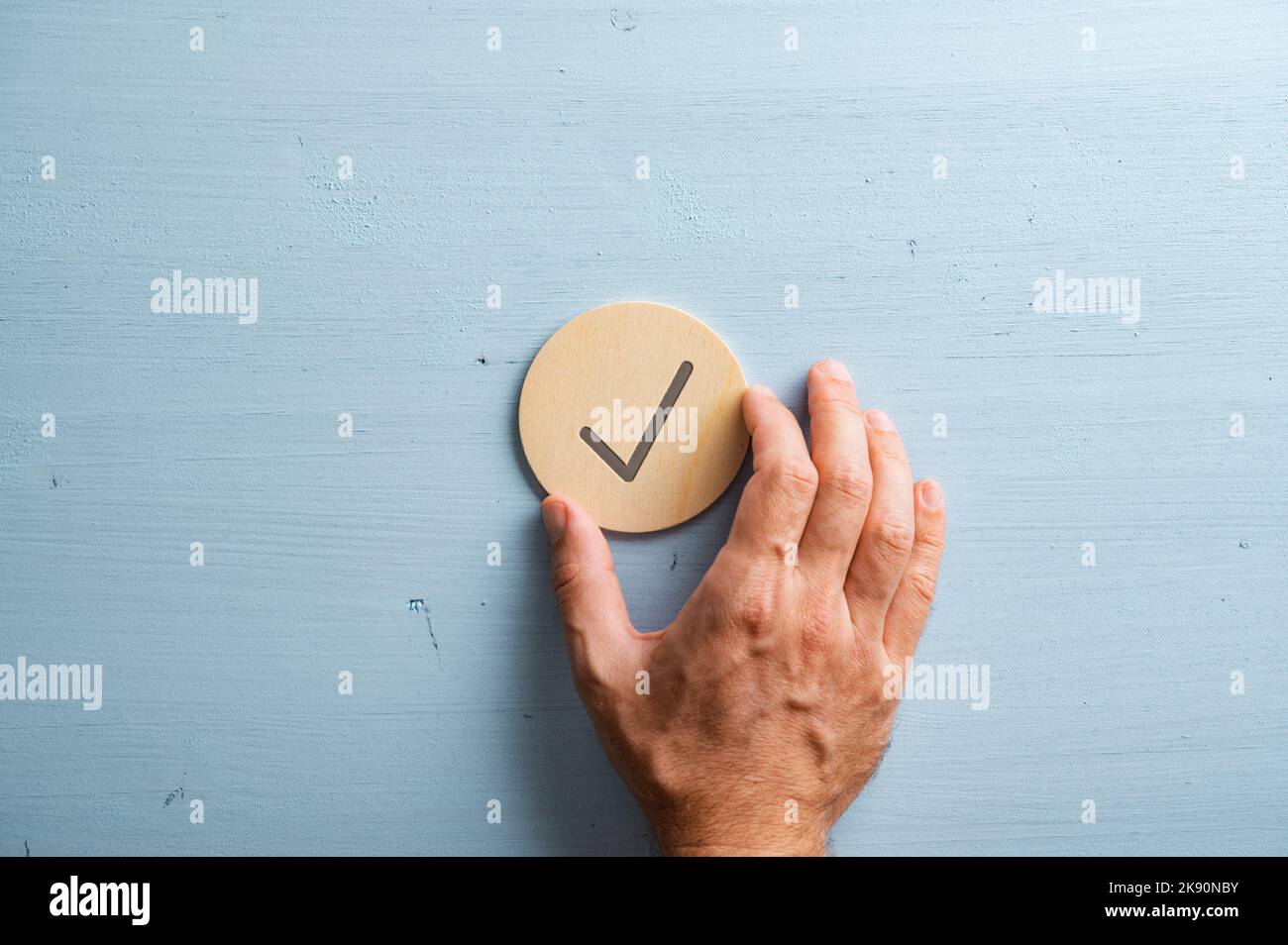 Male hand placing a wooden cut circle with a check mark on it over a ... Male hand placing a wooden cut circle with a check mark on it over a ...