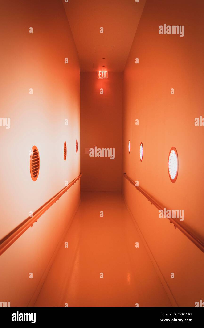 A vertical shot of a narrow corridor with an exit sign and orange ...