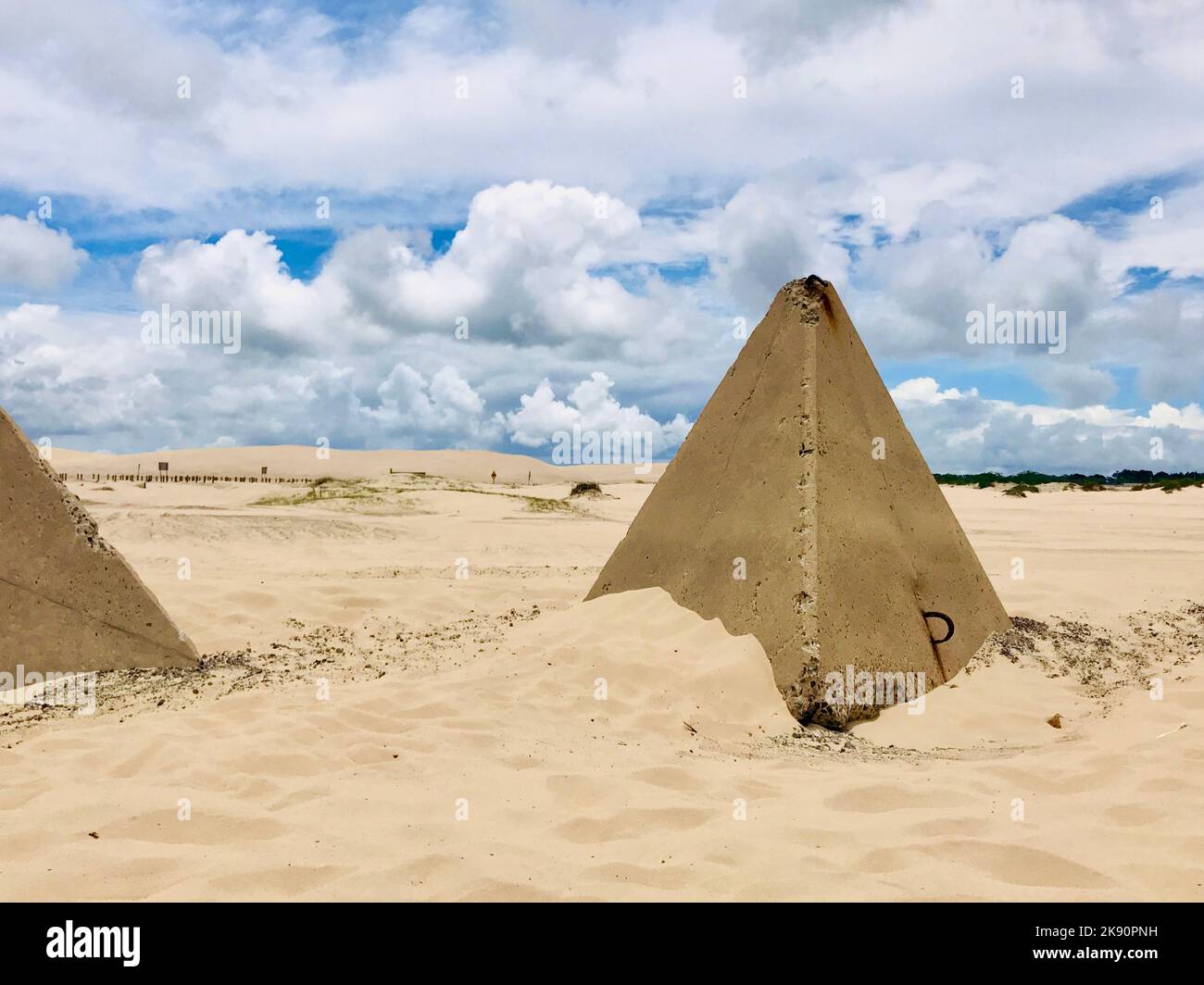 A closeup of a concrete pyramid on a sandy beach with a cloudy blue sky ...