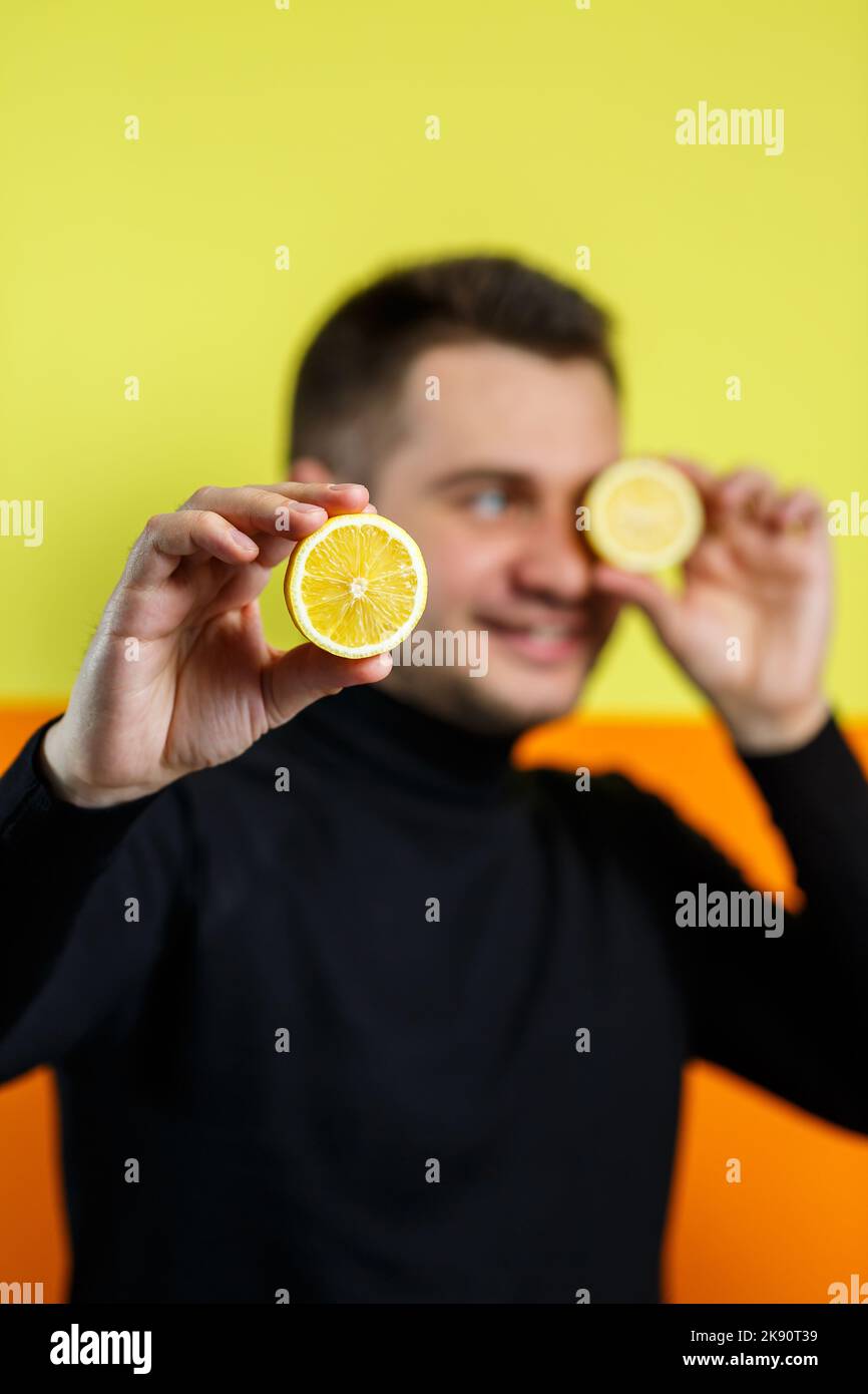 Portrait of a man on a yellow background in black raglan with cut lemon ...